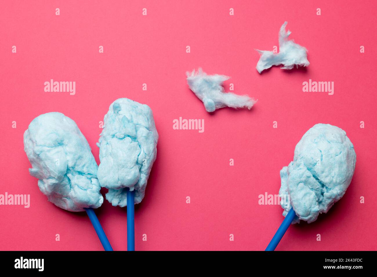 Horizontal image of homemade blue candy floss on three sticks, on pink ...