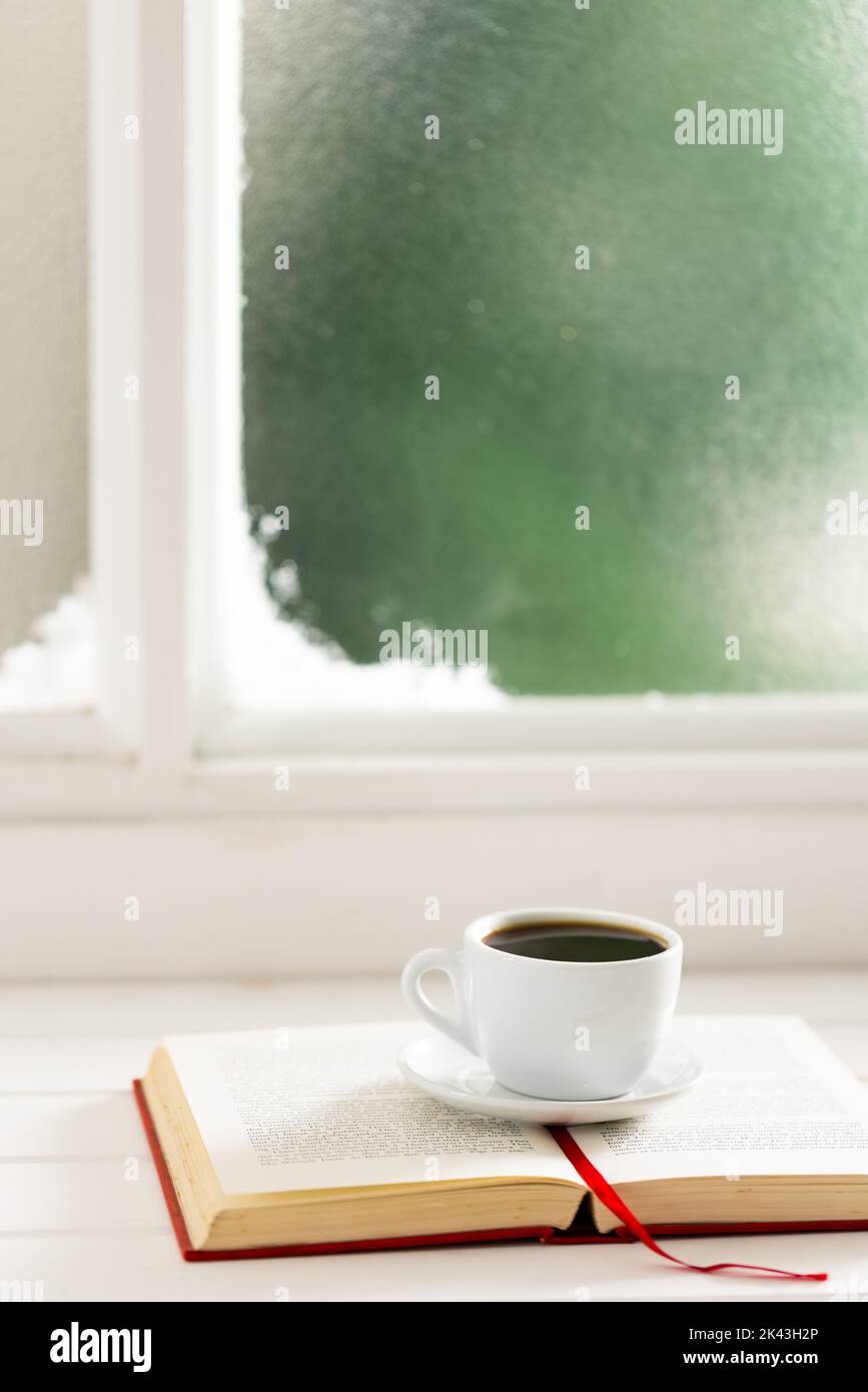 Cup of hot coffee and book over frozen and snowy window Stock Photo - Alamy
