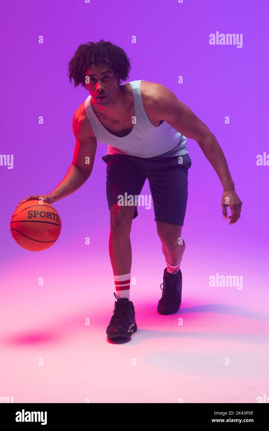 Image of biracial basketball player bouncing basketball on neon purple ...