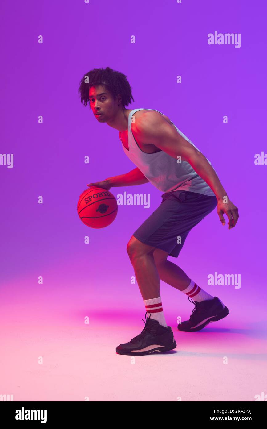 Image of biracial basketball player bouncing basketball on neon purple ...