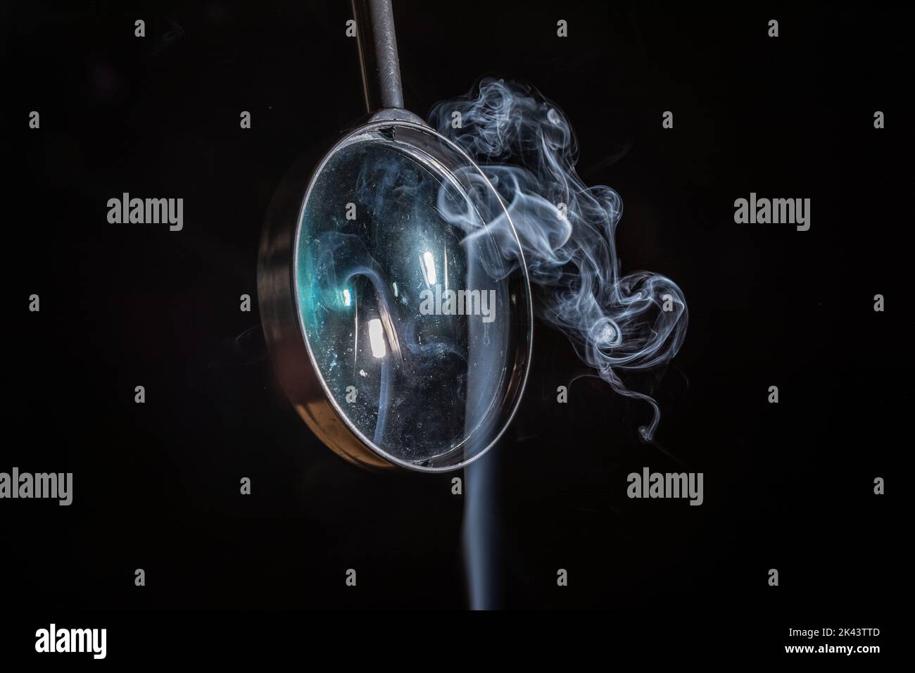 A magnifying glass against a black background and smoke coming from ...