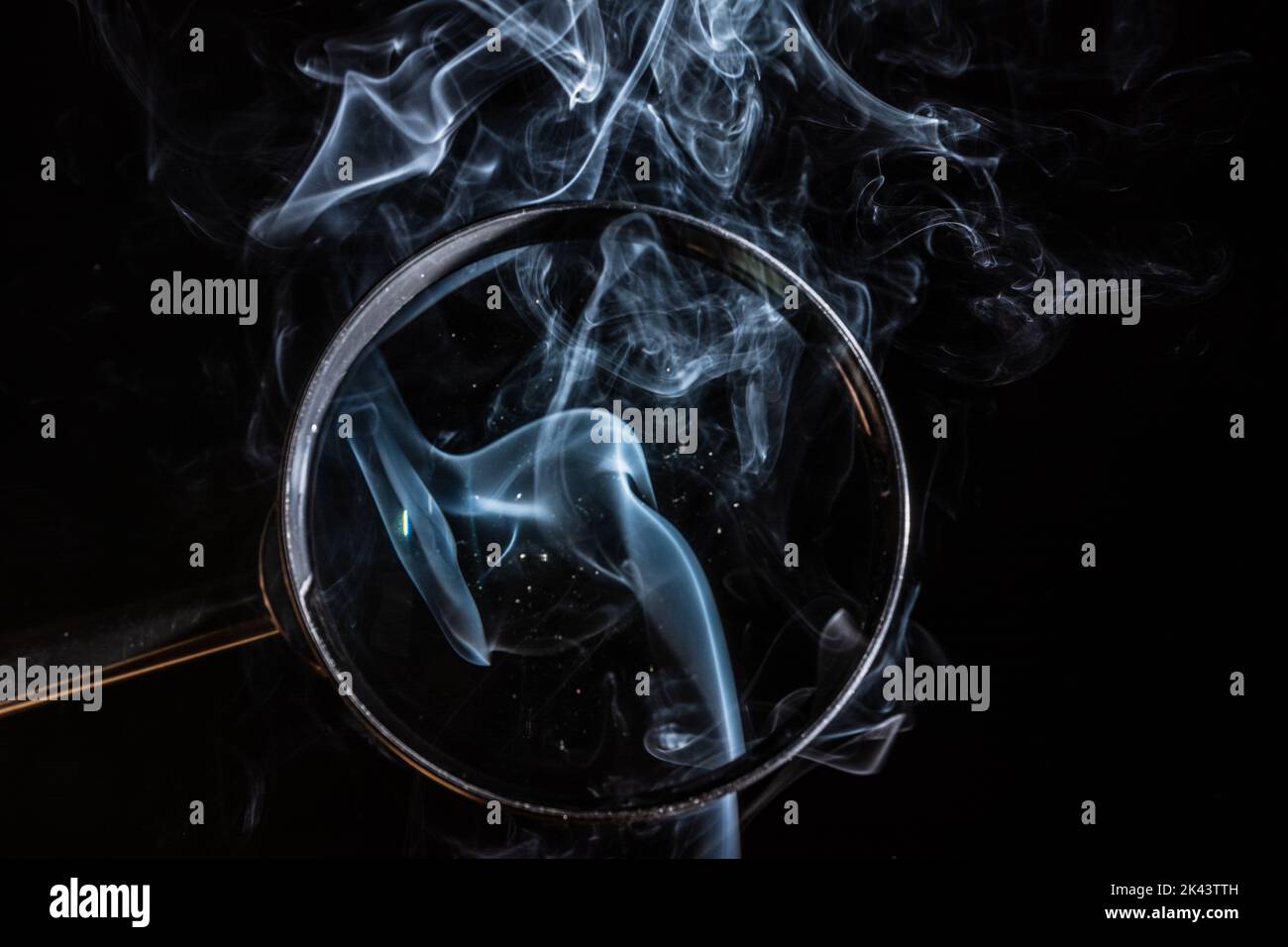 A magnifying glass against a black background and smoke coming from ...