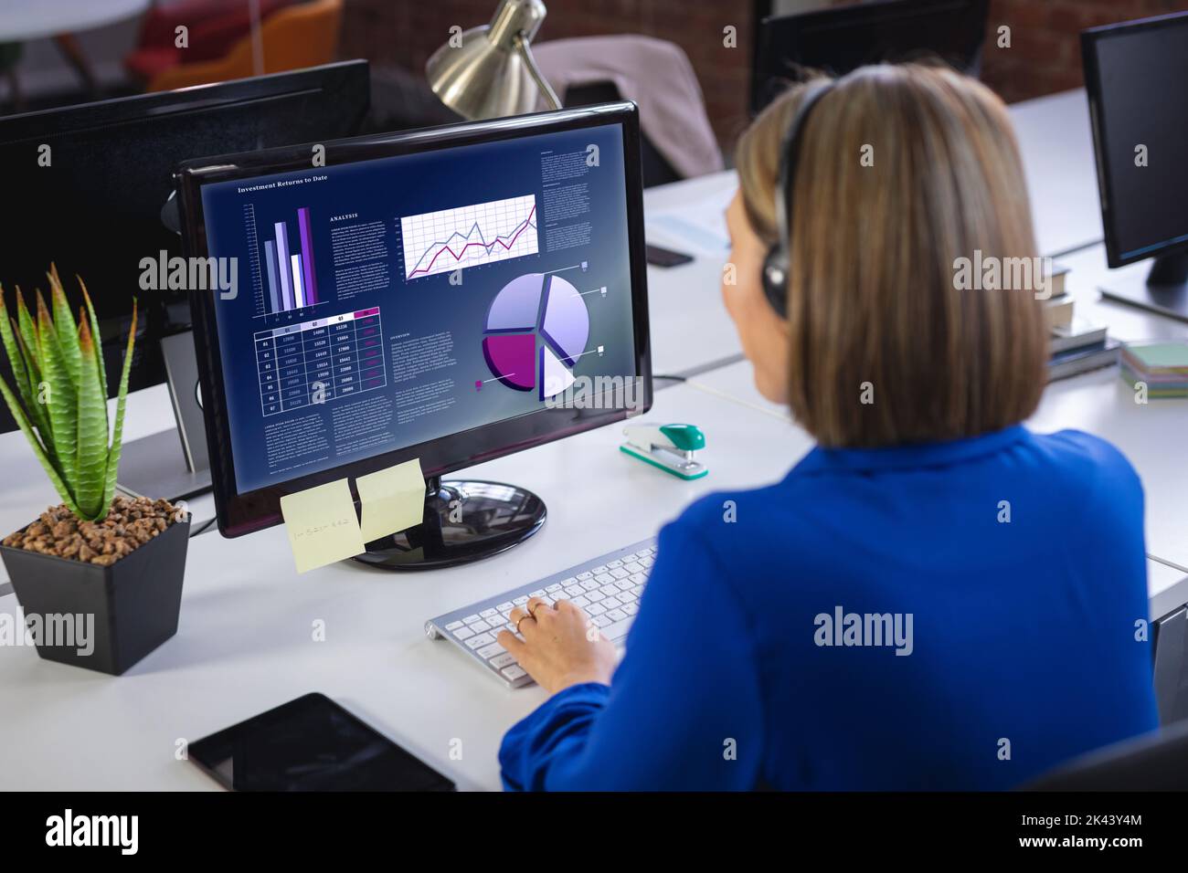 Caucasian businesswoman sitting at desk using computer with statistical ...