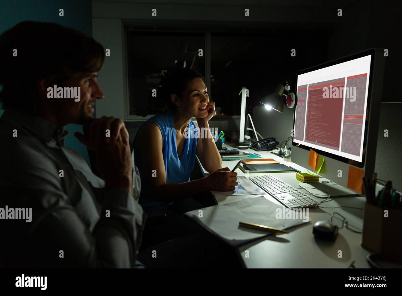 Two diverse male and female colleagues sitting at desk and using computer with coding on screen ...