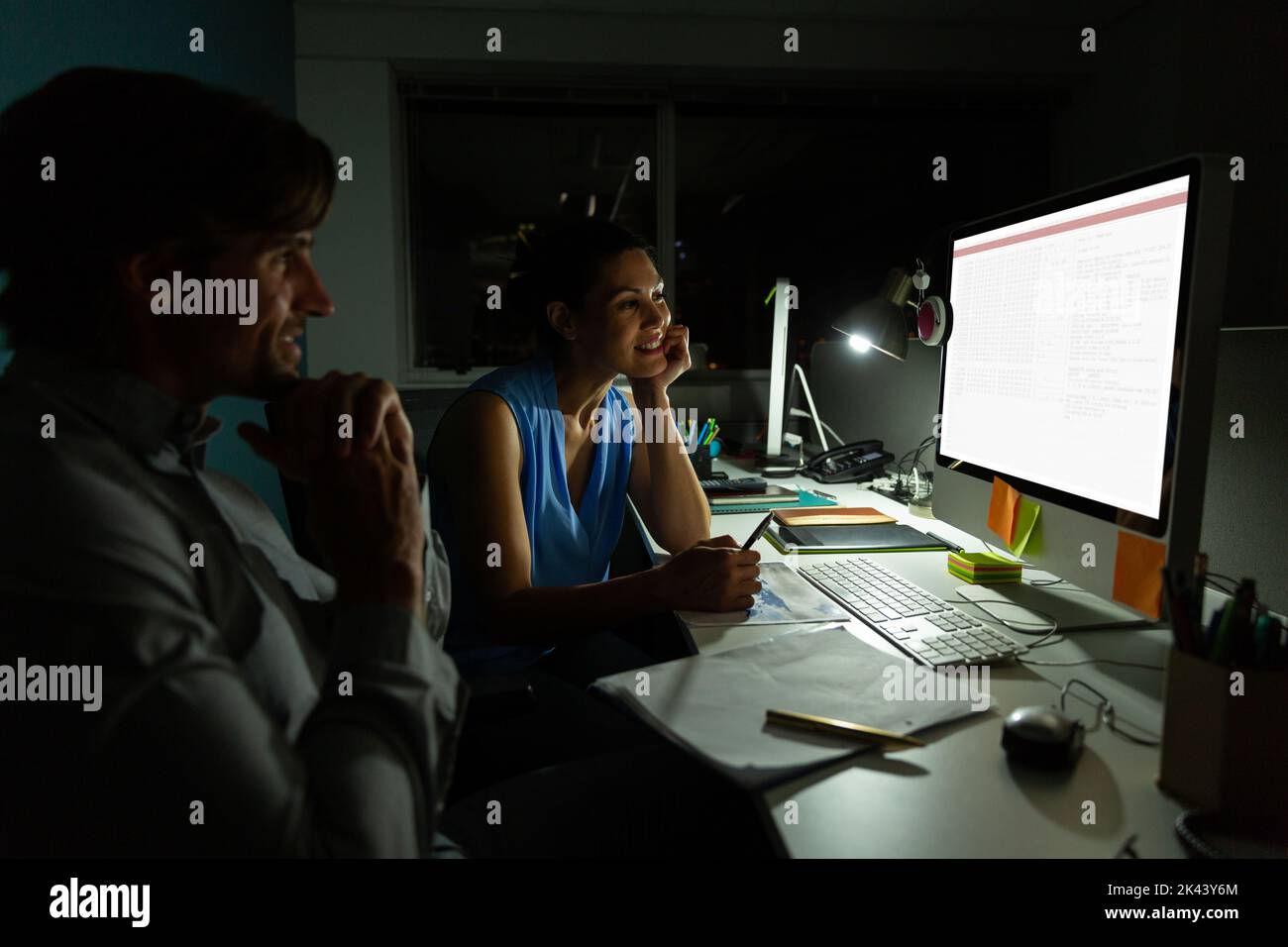 Two diverse male and female colleagues sitting at desk and using computer with coding on screen ...