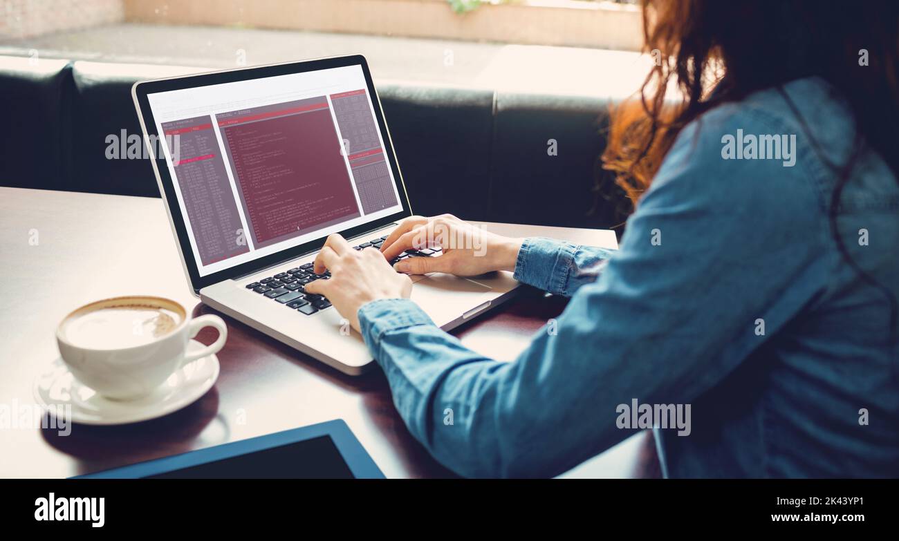 Midsection of caucasian female programmer sitting with coffee, using laptop with coding on ...