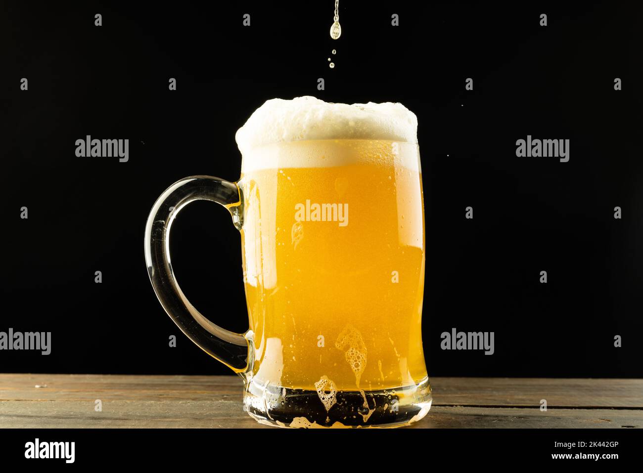 Image of beer pouring into glass tankard of foamy beer on wooden table ...