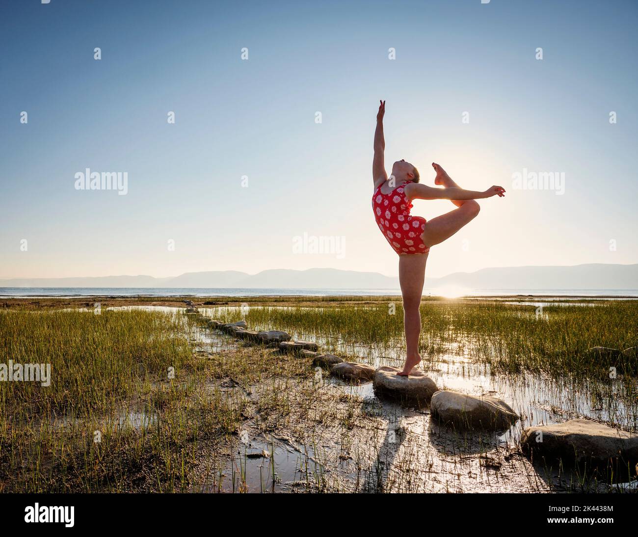 Girl (12-13) in swimsuit performing yoga dance pose on stepping stone ...