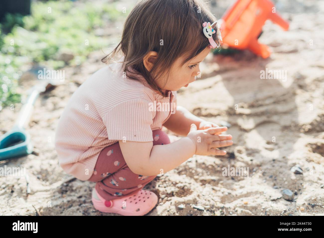 Portrait of an adorable kid girl enjoying playing in sand on the ground ...