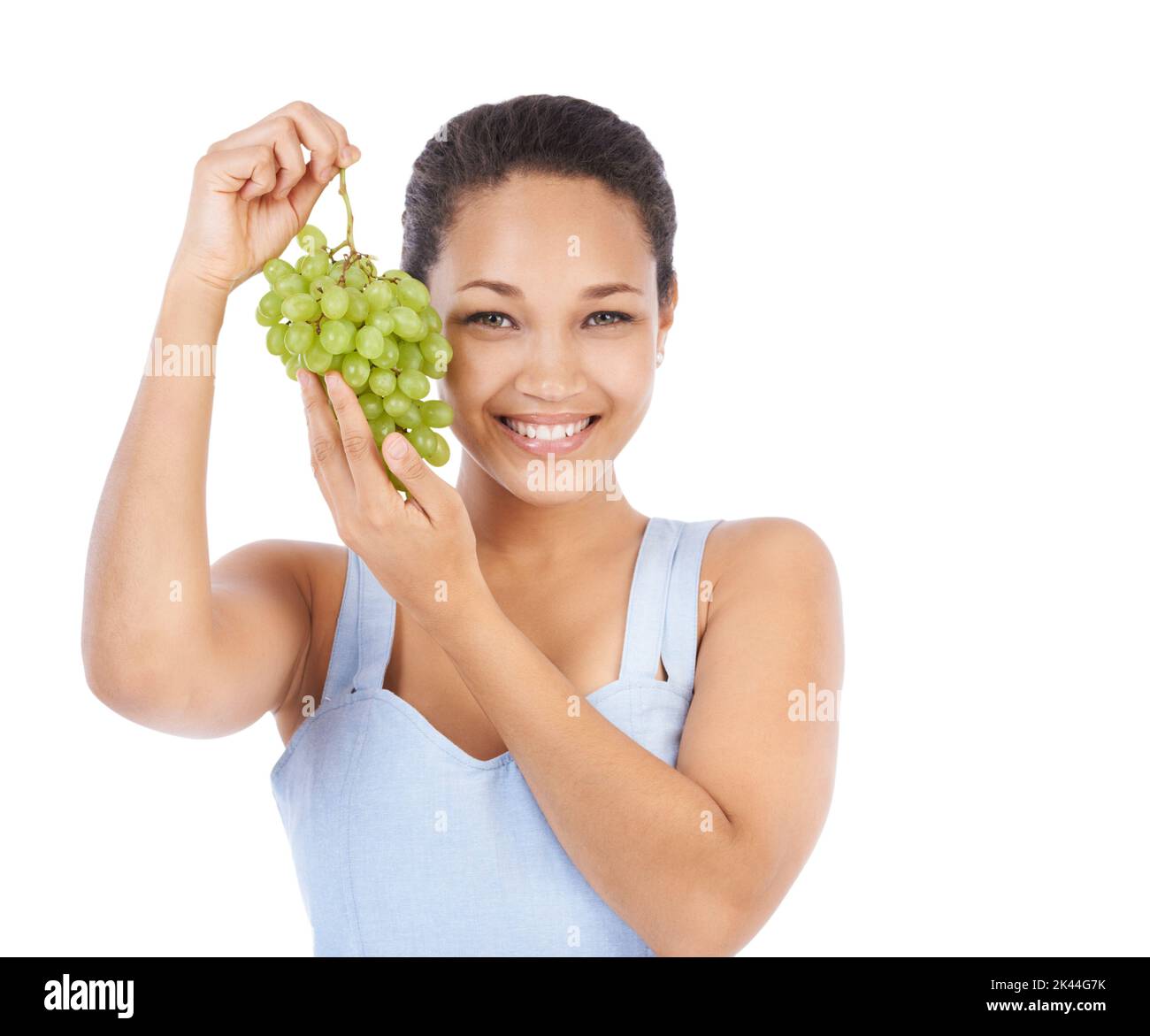 Her favorite fruit by far. Young woman smiling while holding up a bunch of grapes - isolated on ...