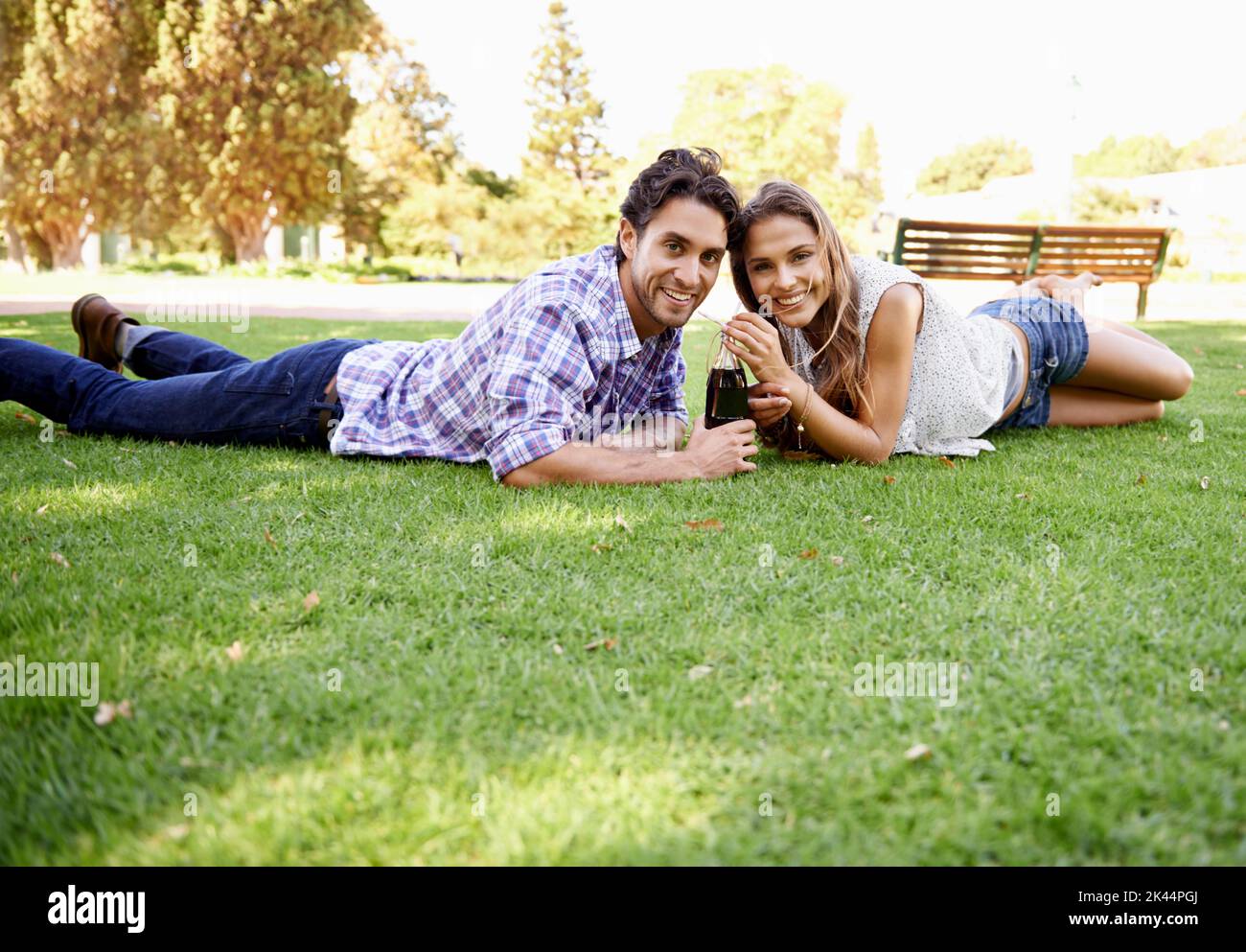 Sharing a soda in the park. A happy young couple sipping cola together ...