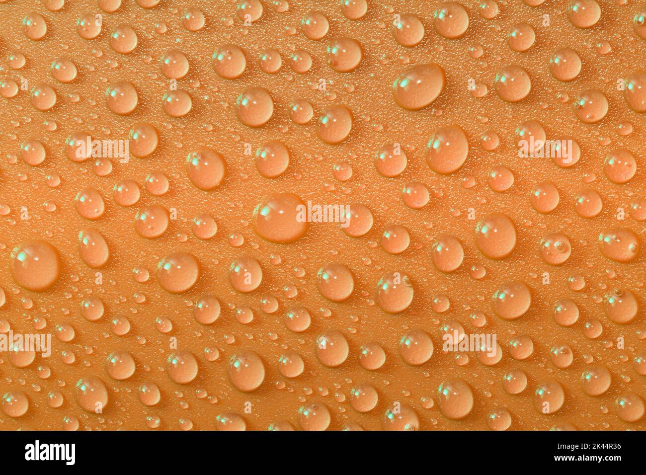 A close-up of orange water droplets on a shiny orange plastic surface ...