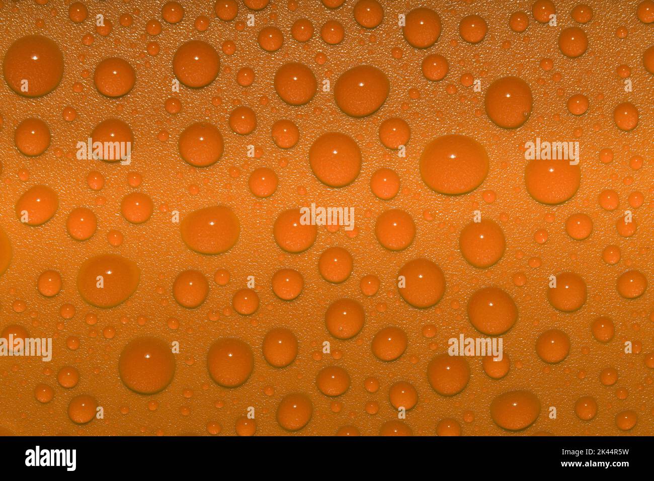 A close-up of orange water droplets on a shiny orange plastic surface ...
