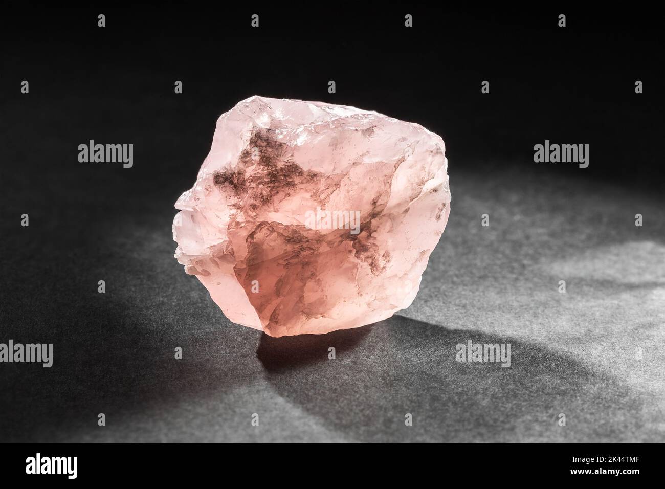 Rough uncut rose quartz specimen, backlit from behind over dark ...