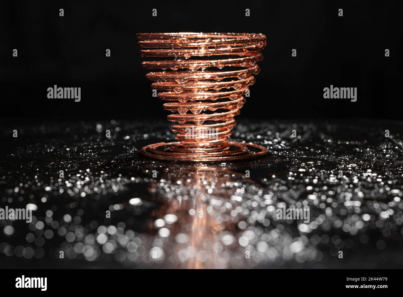 Copper spring holder closeup on the black background on wet surface ...