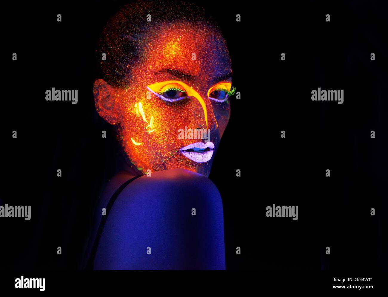 Glowing beauty. A young woman with with neon paint on her face posing ...