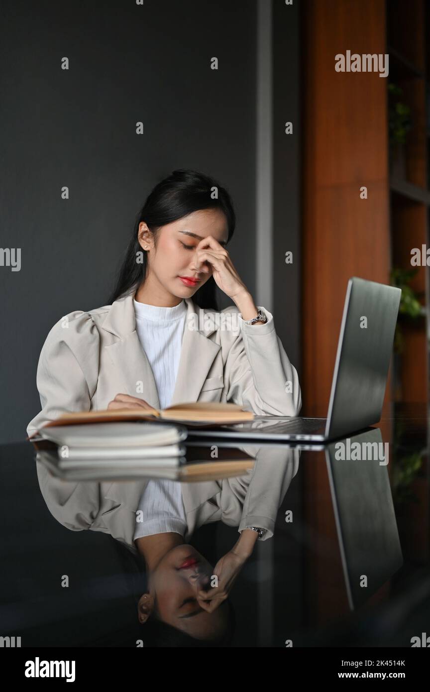 Stressed millennial Asian businesswoman or female manager at her desk ...