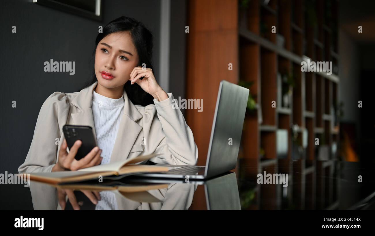 Thoughtful, stressed and worried millennial Asian businesswoman or female manager holding her ...