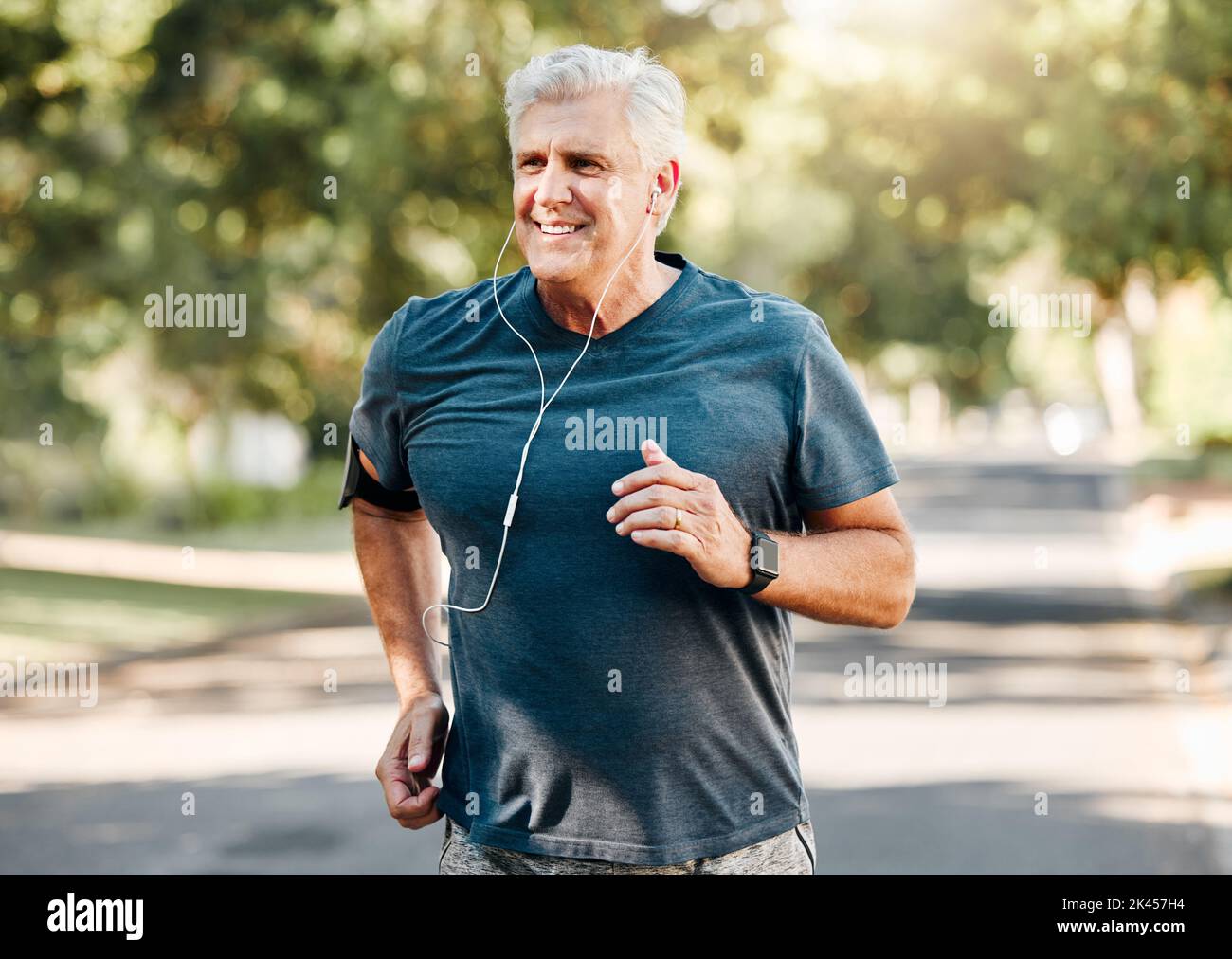 Senior man running while listening to music outdoor street and park for ...