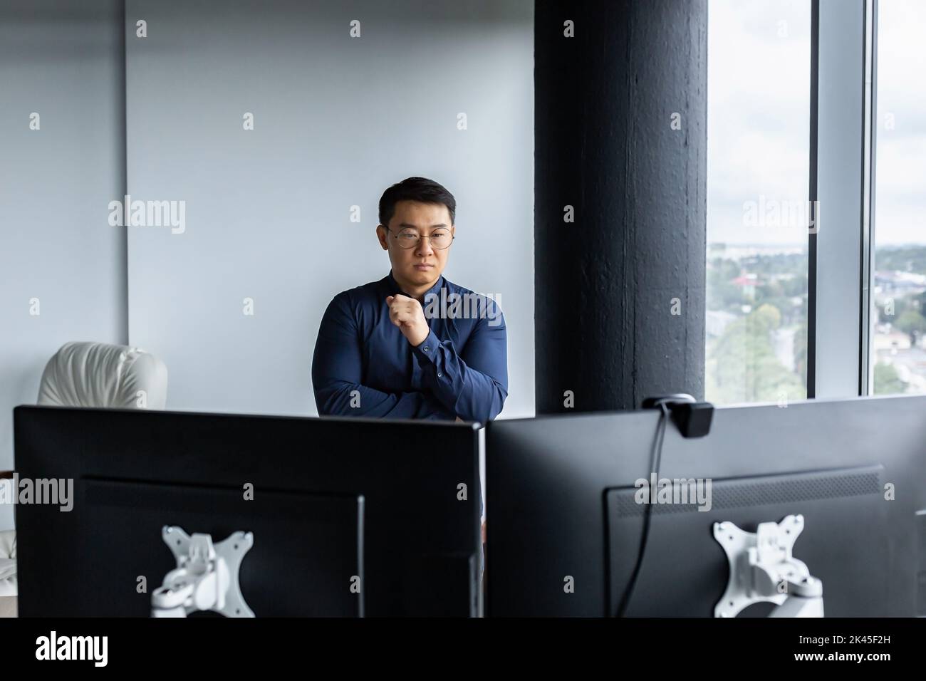 Serious and thinking asian engineer looking at two monitors, close-up ...