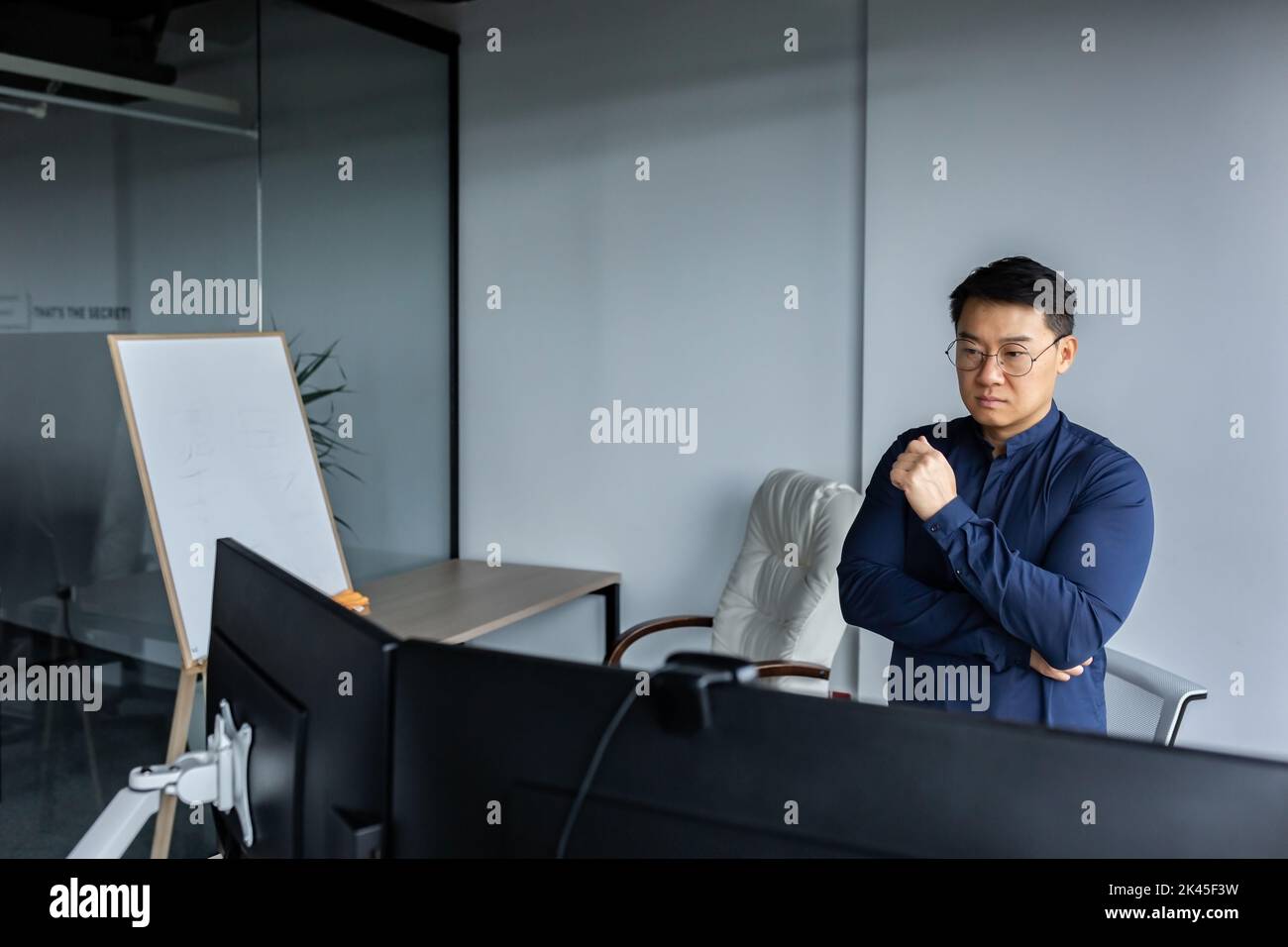 Serious and thinking asian engineer looking at two monitors, close-up ...