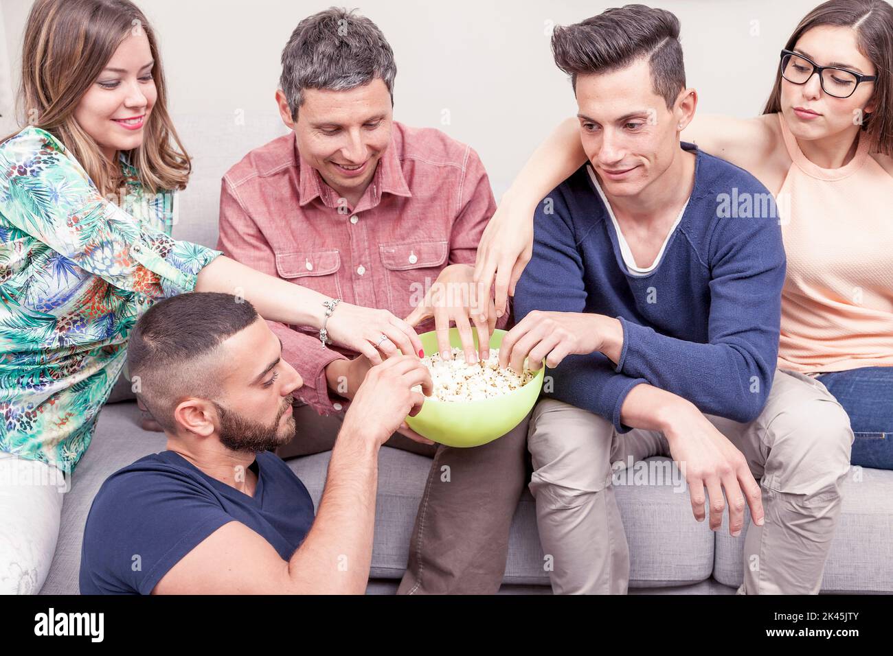 group of friends eating popcorn on sofa Stock Photo - Alamy