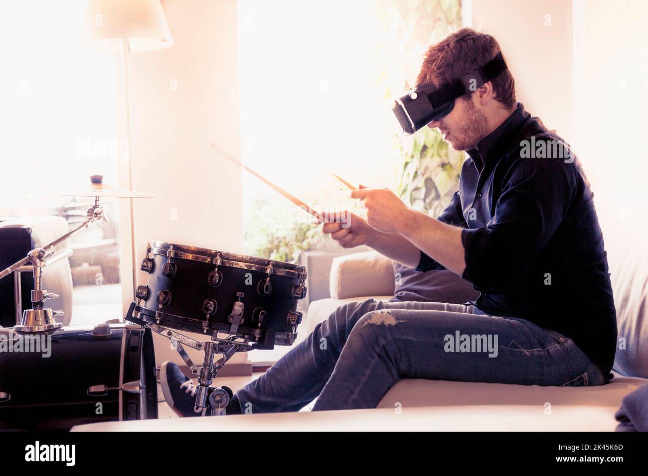 young adult playing drums at home using viewer for virtual reality ...