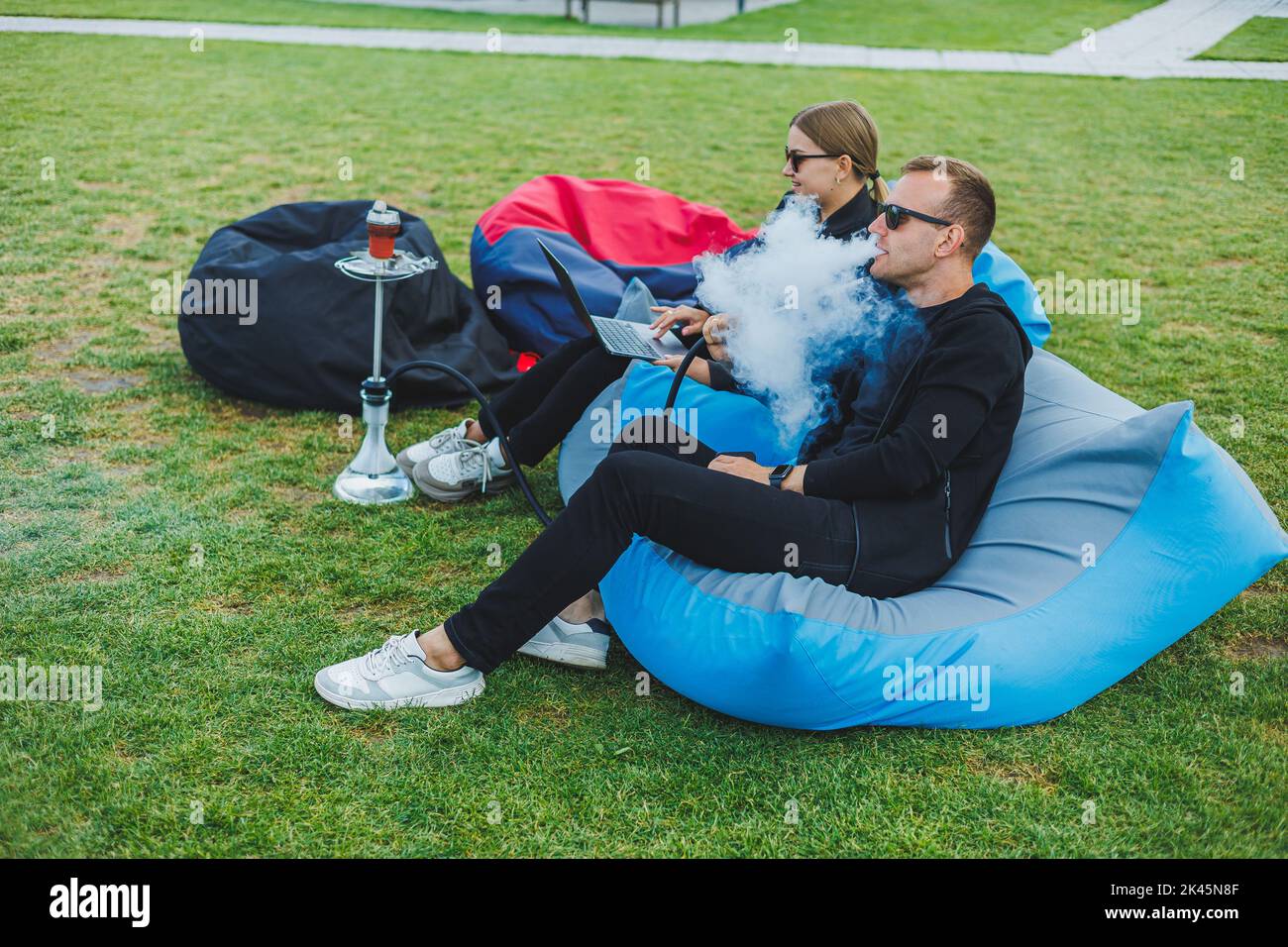 A young couple relaxes in the park and smokes hookah. A man and a woman ...