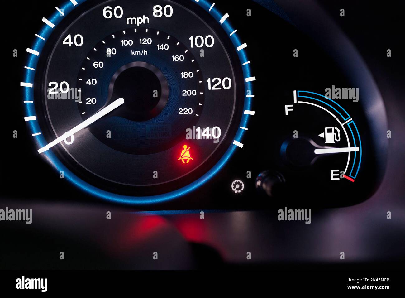 A lit up car dashboard, mph speed dial, in miles and kilometres, fuel guard and a red warning ...