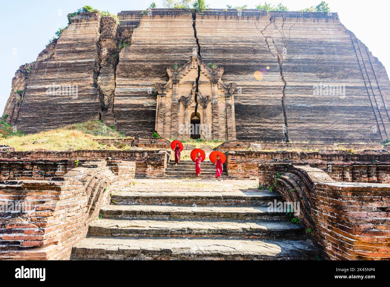 Three monks with orange umbrellas outside a large rock temple, the ...