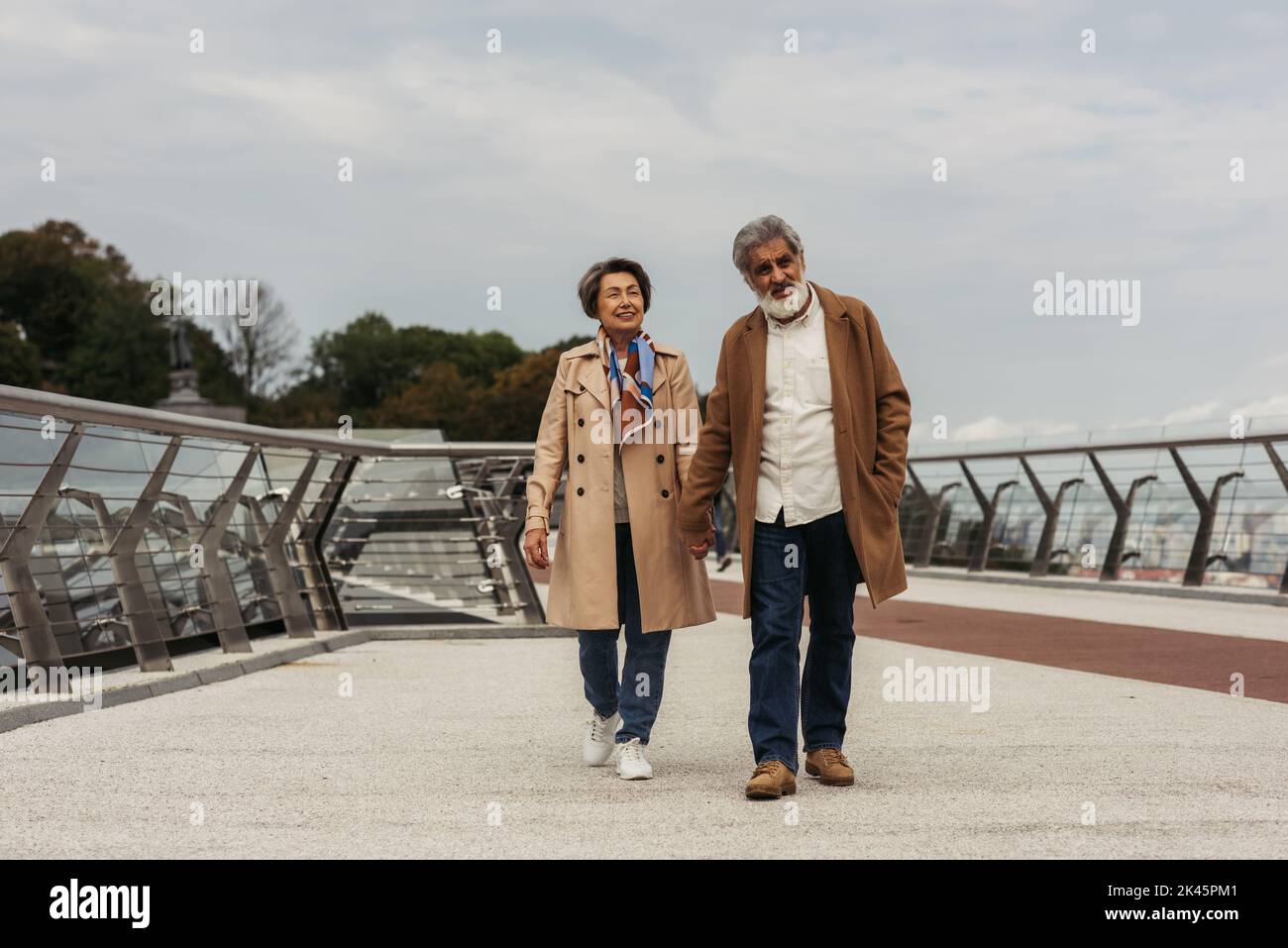 full length of happy senior couple in coats holding hands and walking ...