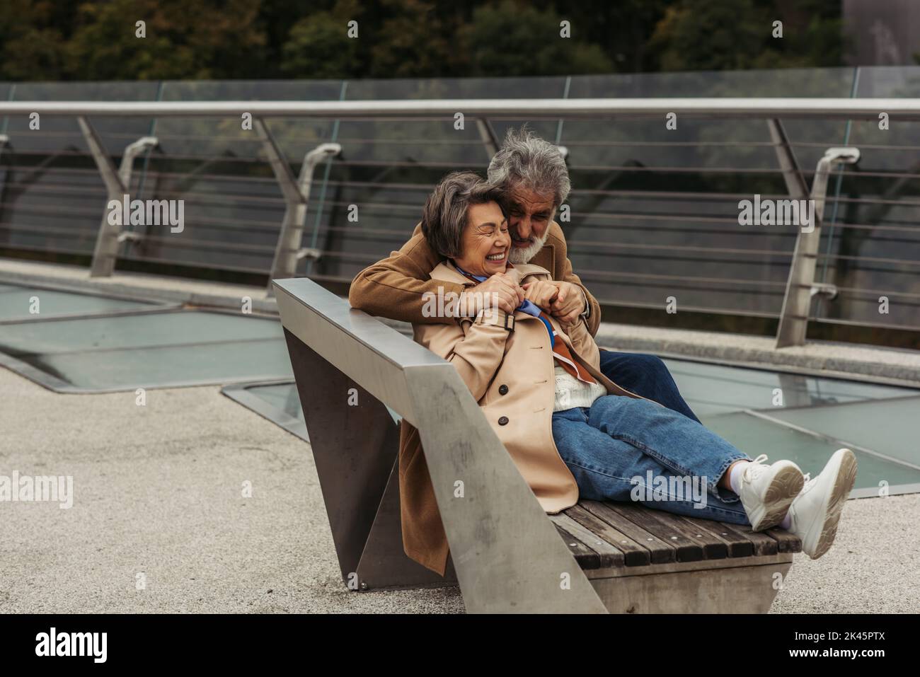 happy senior man hugging positive wife while sitting on bench near ...