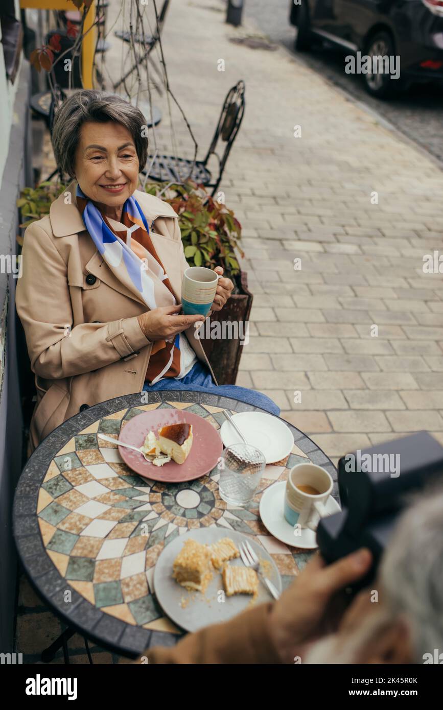high angle view of man taking photo of happy senior wife with cup on ...