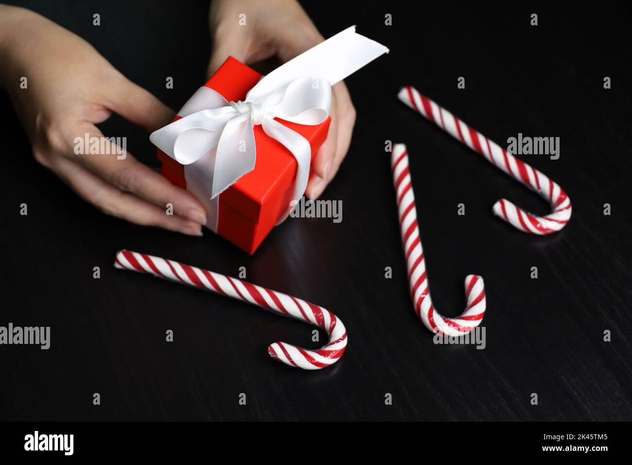 Red gift box in female hands on dark wooden table with candy canes ...