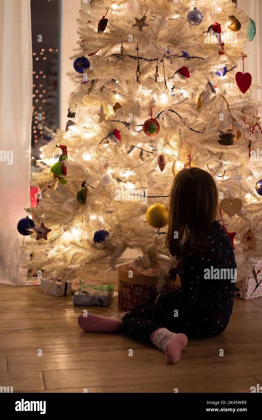 Child girl, back view, sitting in pajamas near a white illuminated ...