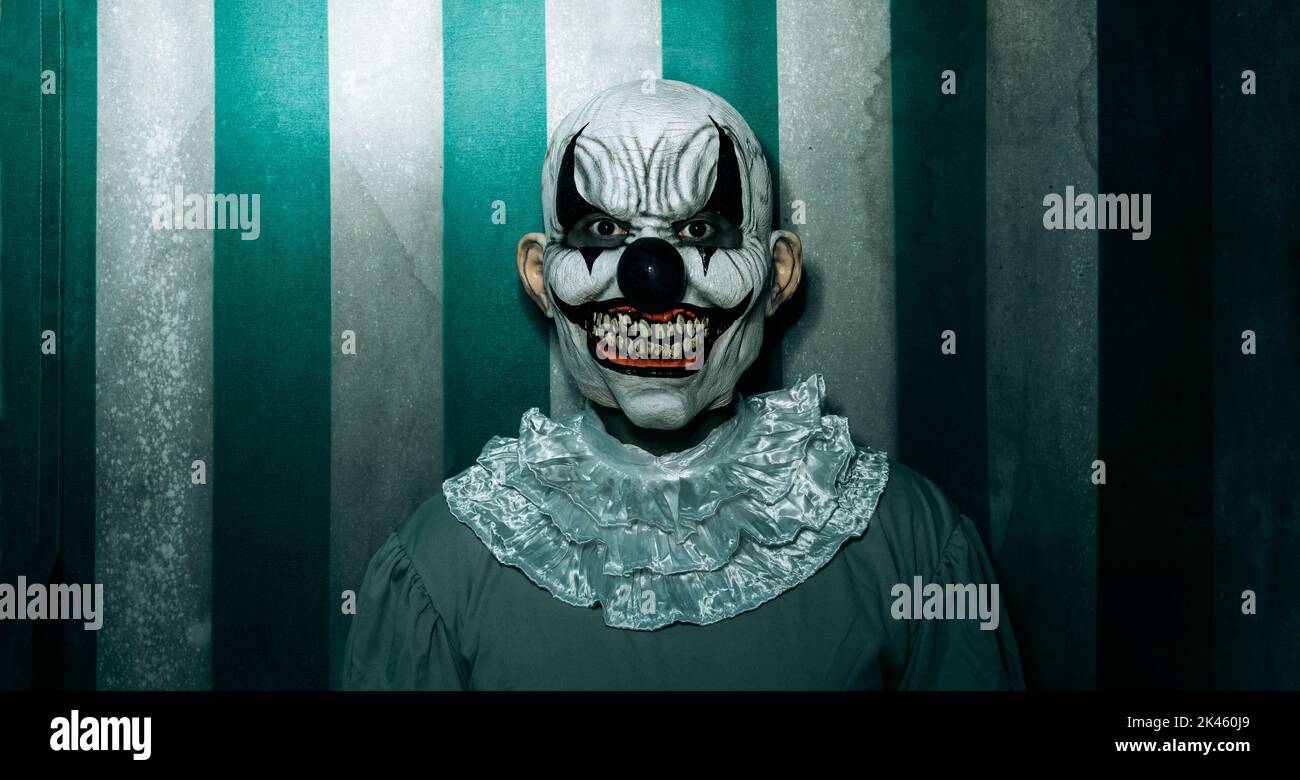closeup of a creepy evil clown, in a gray costume with a white ruff, in ...