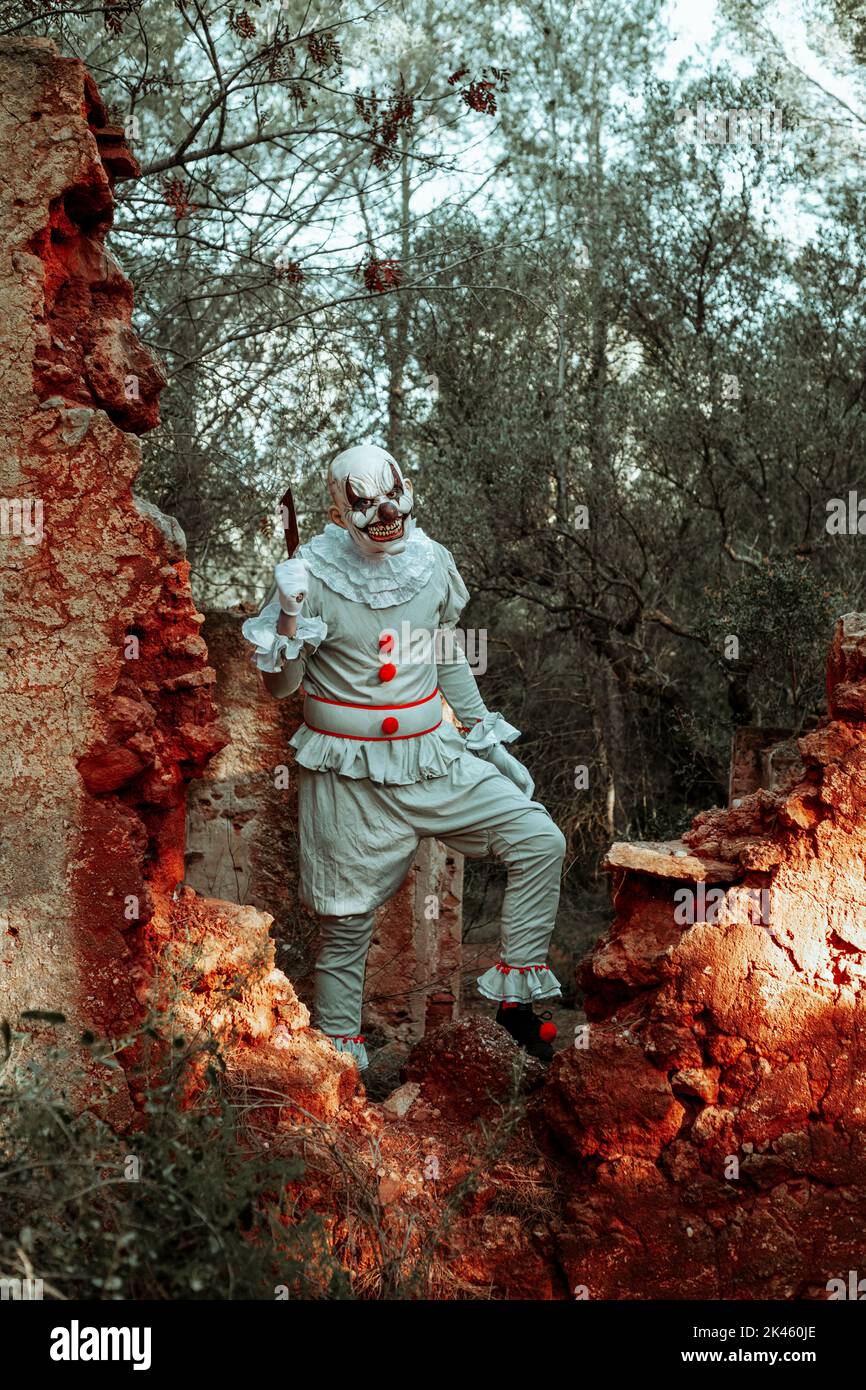 a creepy evil clown, wearing a gray costume with white ruffles, and ...