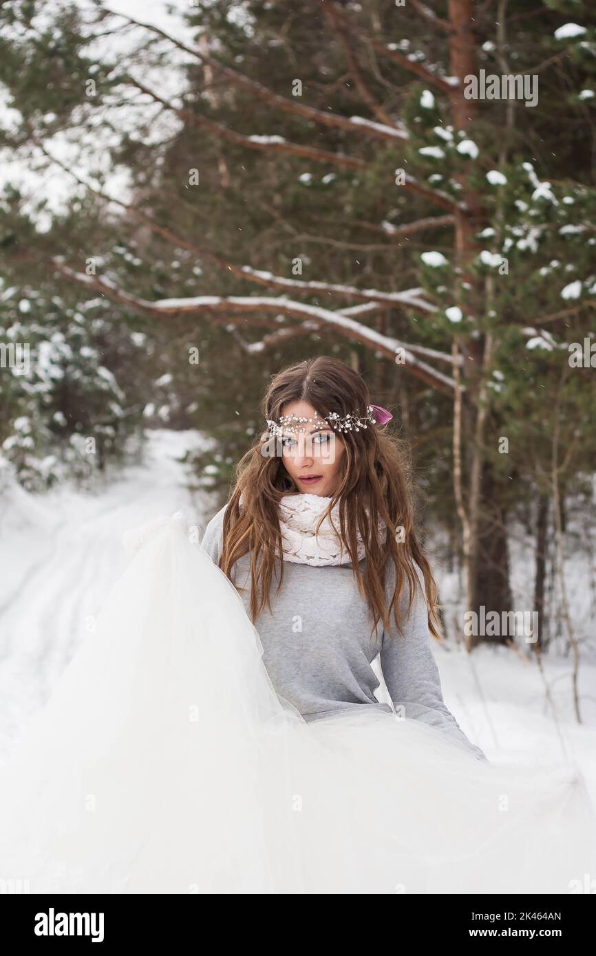 Beautiful bride in a white dress with a bouquet in a snow-covered ...