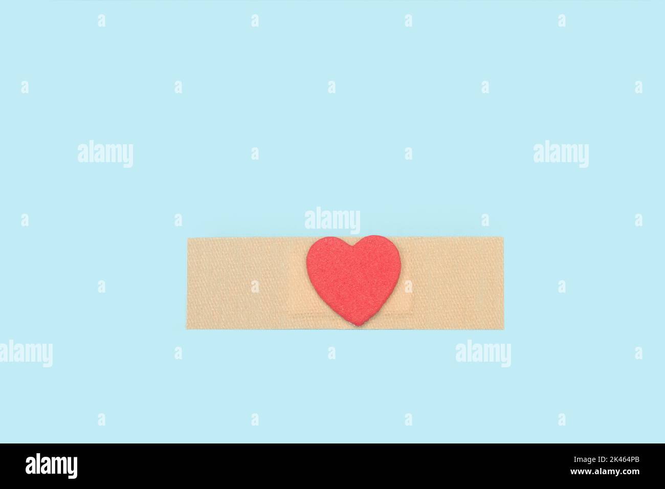 A red paper heart on an adhesive bandage on a light blue background ...