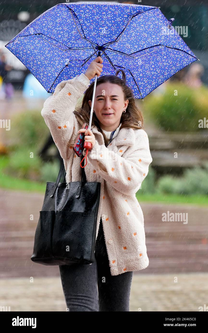A woman struggles with her umbrella during the wet and windy weather in ...