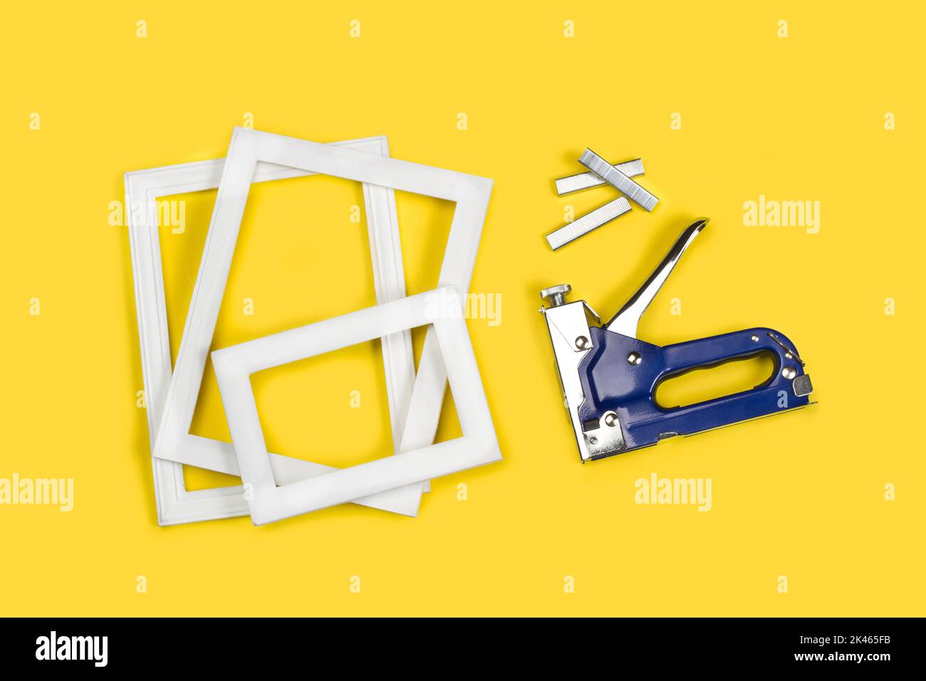 A blue stapler gun, staples and photo frames on a yellow background ...