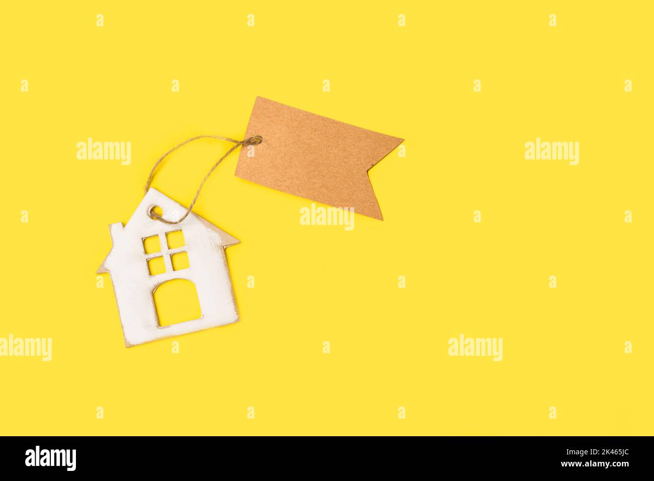 A cardboard house with a brown blank paper label on a yellow background ...