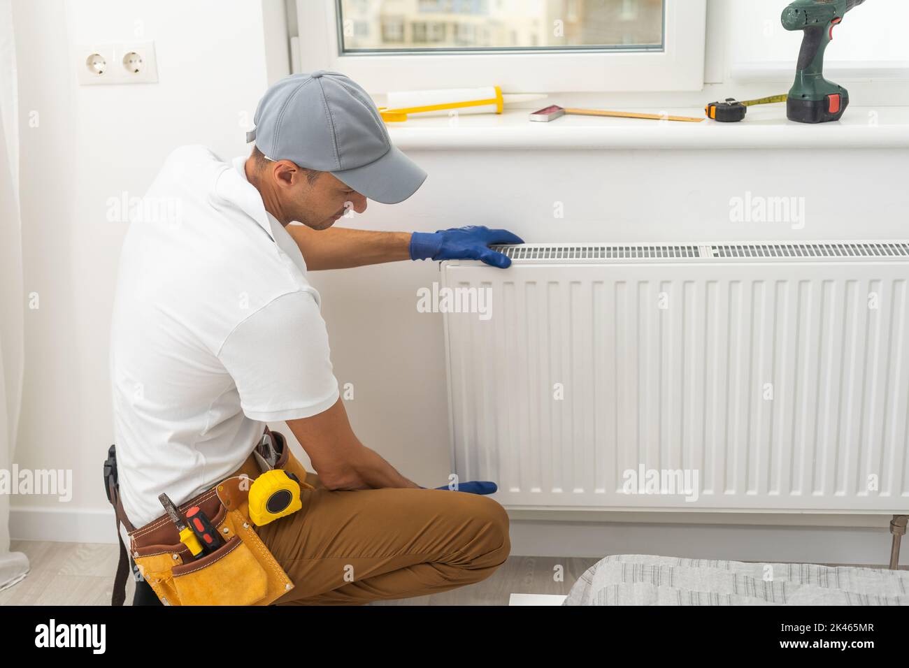 A male plumber installs a radiator in the heating system of an ...