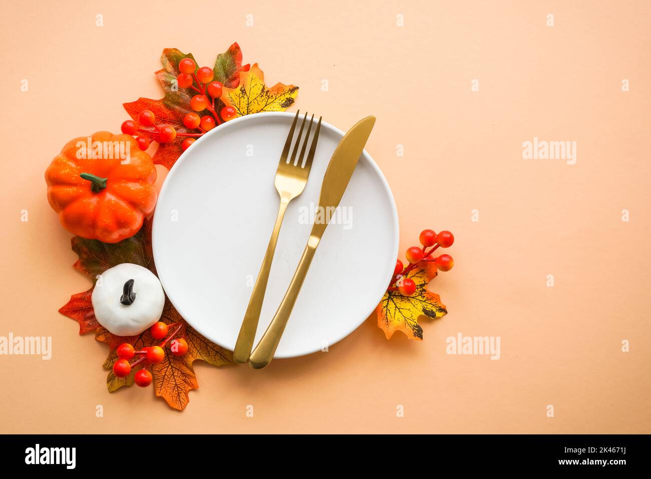 Autumn table setting. White plate, golden cutlery and fall decorations ...