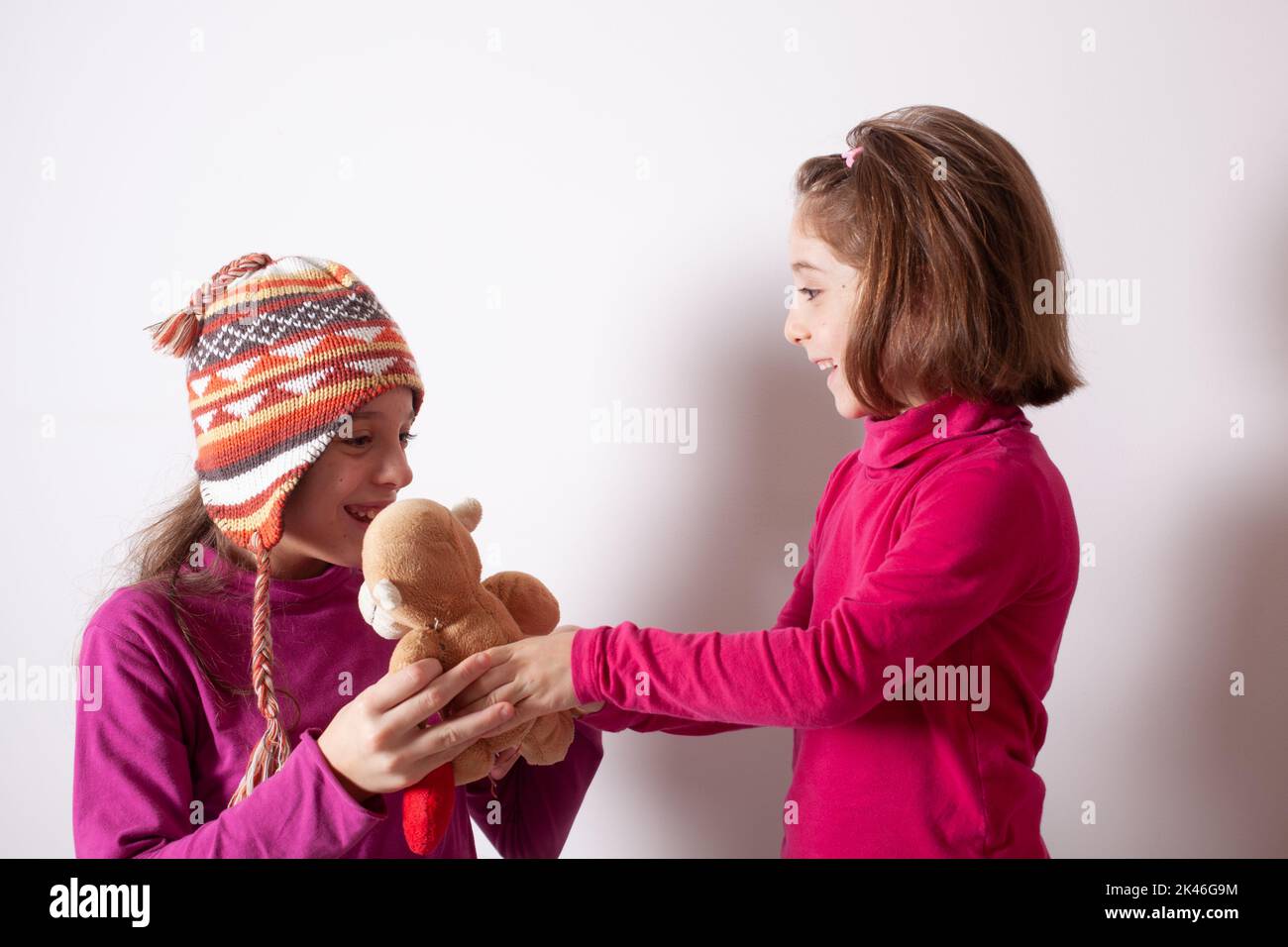 Little girl giving her teddy bear toy to older sister. Cute child girl ...