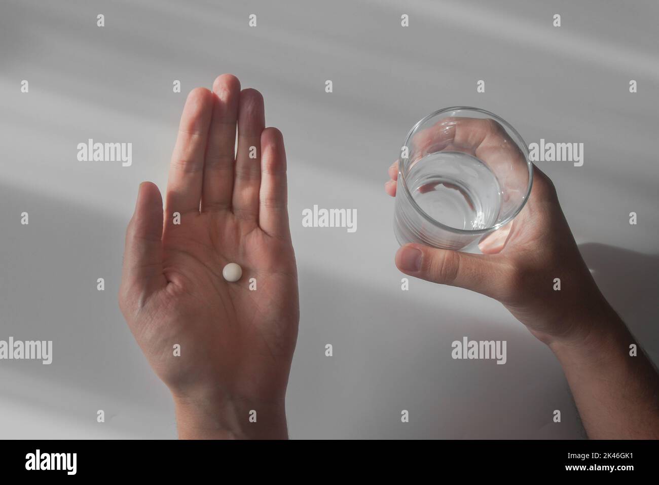 Male hand on white background holds a white pill and a glass of water ...