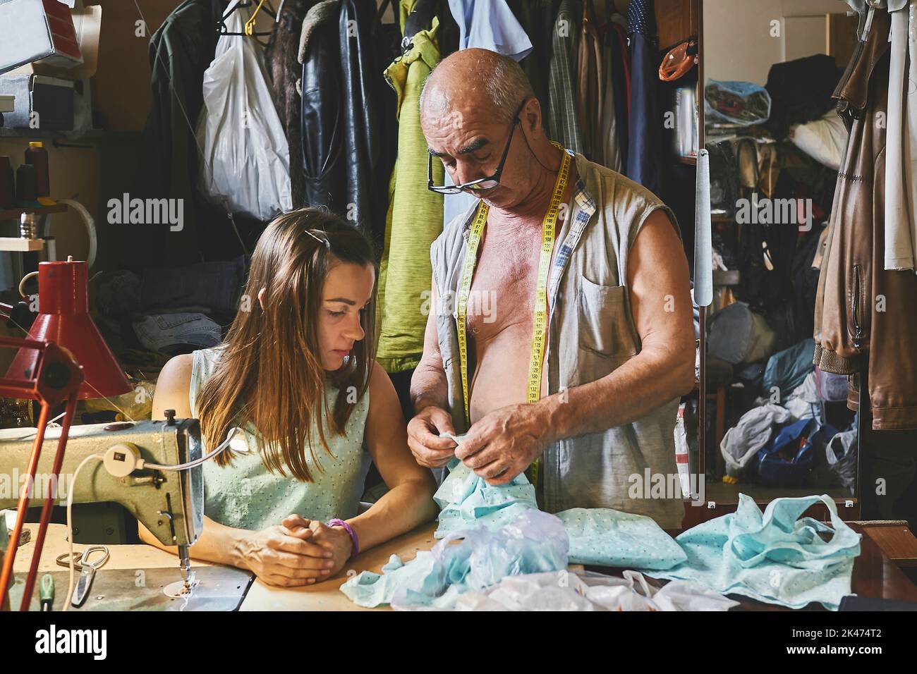 Senior experienced master tailor teaches a young girl seamstress how to ...