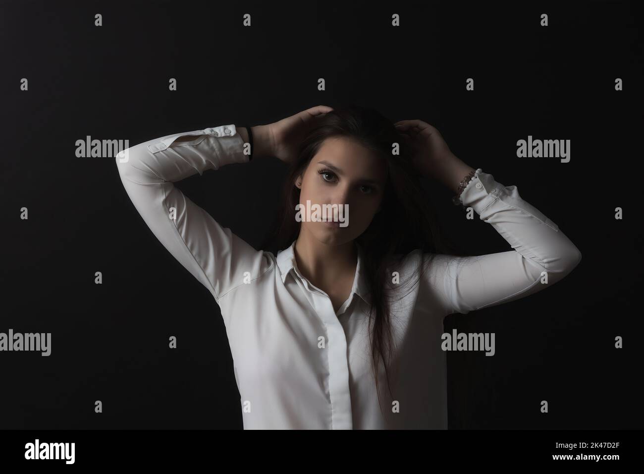 Low key portrait of beautiful young woman posing with both hands in her ...