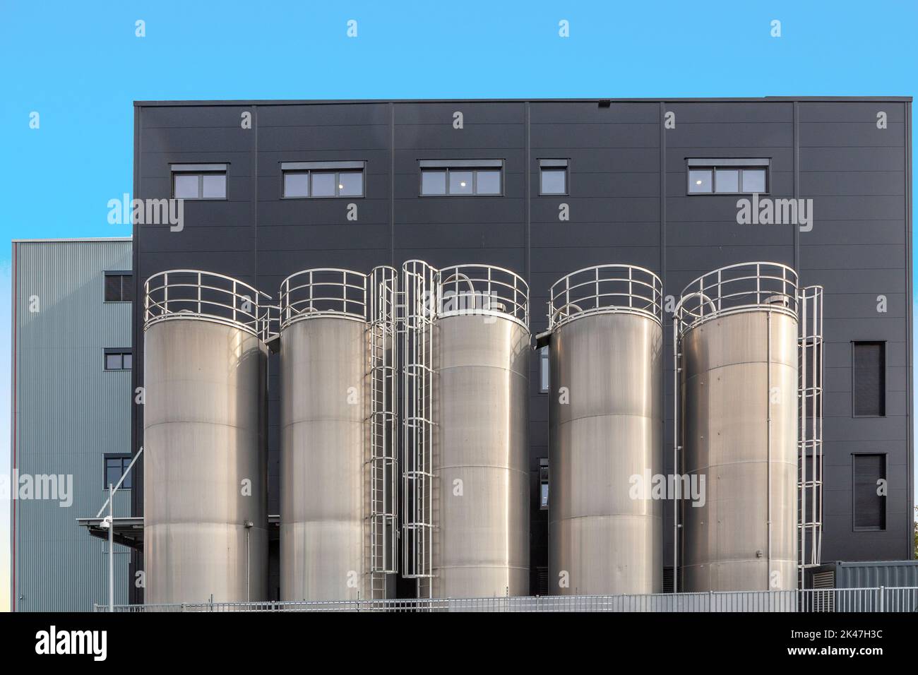 chrome silos in front of generic grey wall of a plant under blue sky ...