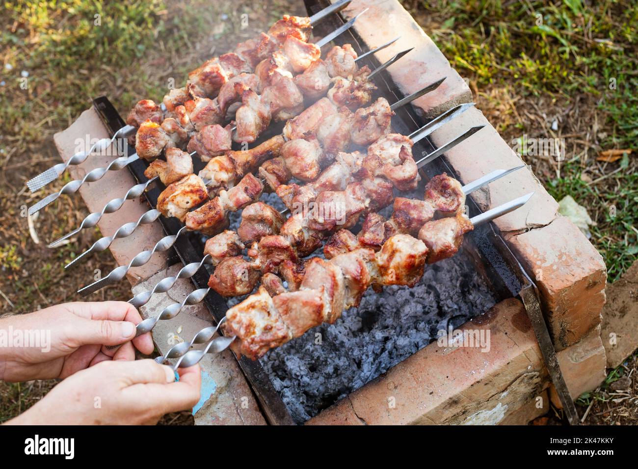A man flips pork skewers grilled over coals on a brick grill. Delicious ...